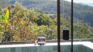 Vista da janela para uma piscina, com paisagem montanhosa ao fundo.