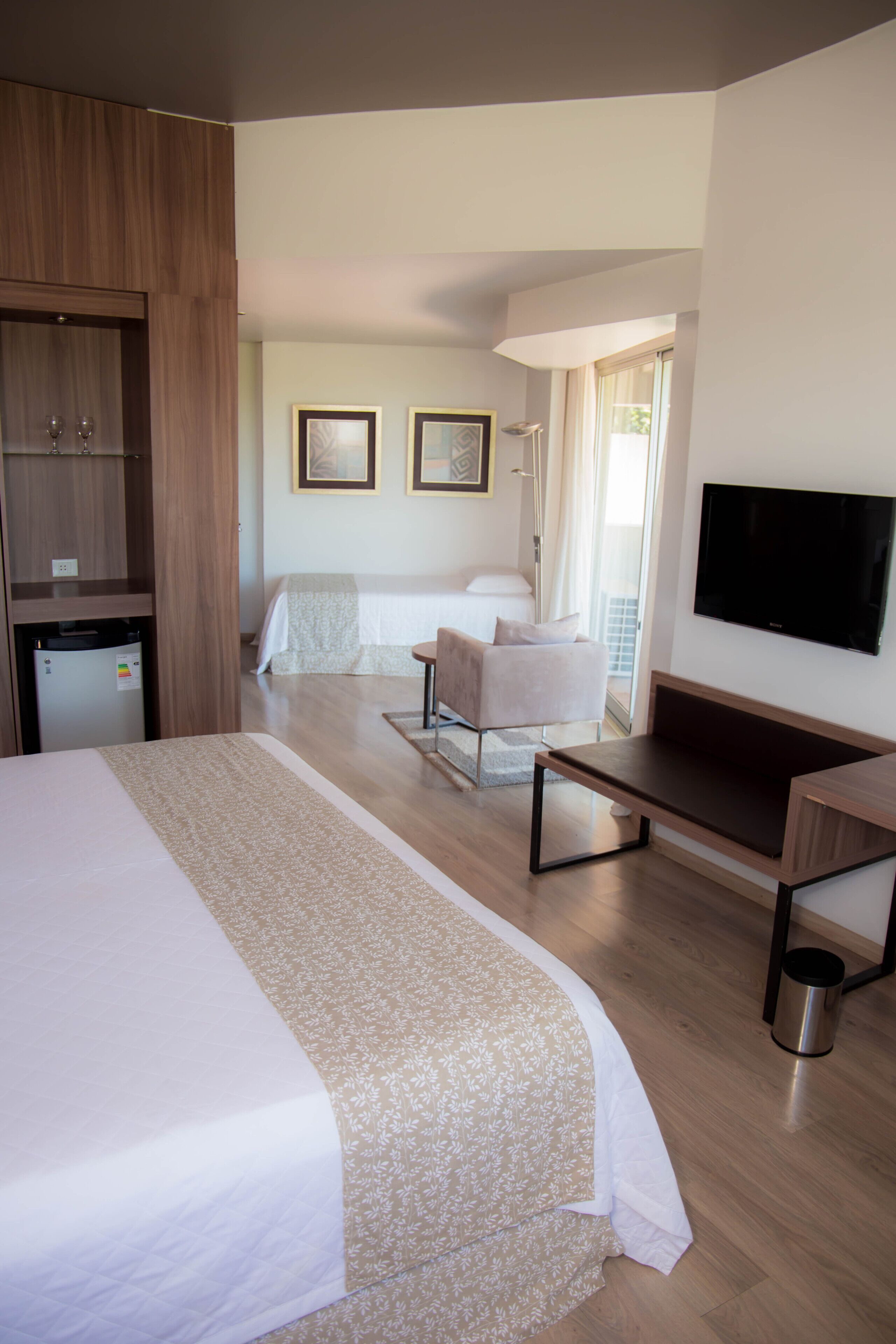 Quarto de hotel com uma cama grande, uma escrivaninha, uma cadeira, uma televisão e um guarda-roupa.