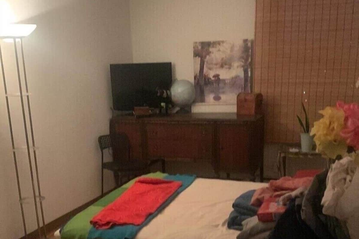 Quarto com cama, escrivaninha, cadeira, televisão e um quadro na parede.