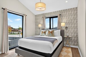 Quarto com uma cama grande, duas luminárias de cabeceira, vista para a rua e parede estampada.