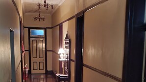 Um corredor com piso de madeira, um candelabro, um espelho e uma porta no final.