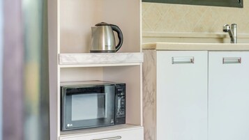 Uma cozinha com micro-ondas e chaleira numa prateleira, e uma pia com torneira.