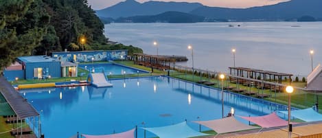 Uma piscina com escorrega, espreguiçadeiras e vista para o mar e montanhas.