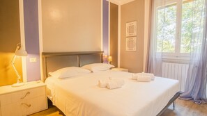 Quarto de hotel com uma cama, mesas de cabeceira, abajur e janela com cortinas.