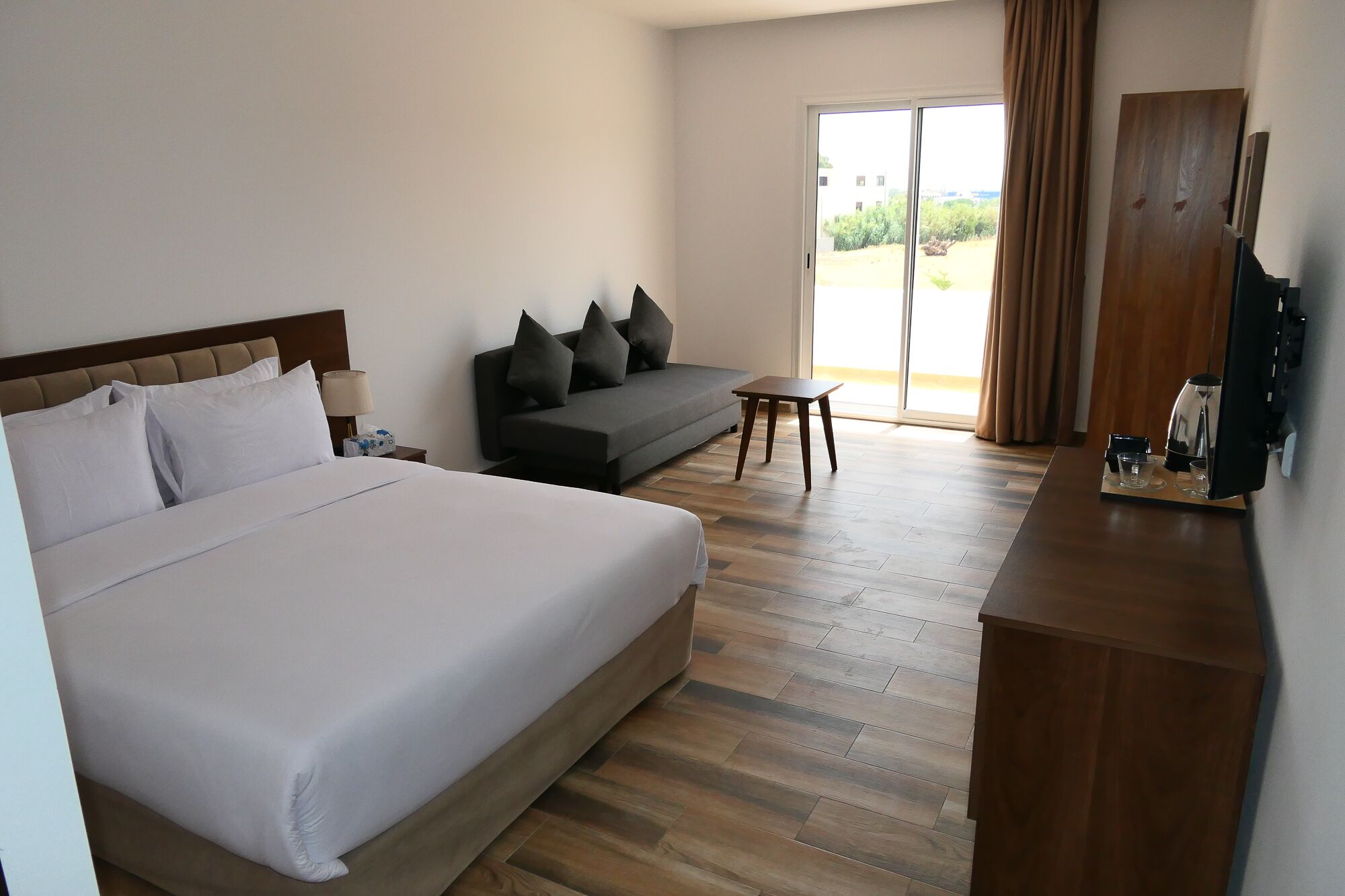 Quarto de hotel com uma cama grande, um sofá, uma mesinha e uma televisão.
