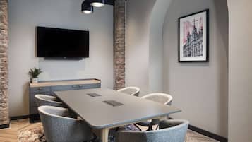 Uma sala de conferências com uma mesa comprida, seis cadeiras, uma TV de tela plana, um quadro com uma vista urbana emoldurada e um pilar de pedra.