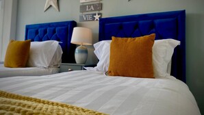 Uma cama de casal bem arrumada, com almofadas brancas e mostarda, uma cabeceira azul e uma parede com estrelas e placas decorativas.