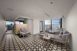 Uma sala de estar moderna com piso xadrez, um sofá, uma poltrona e vista para a cidade através de grandes janelas.