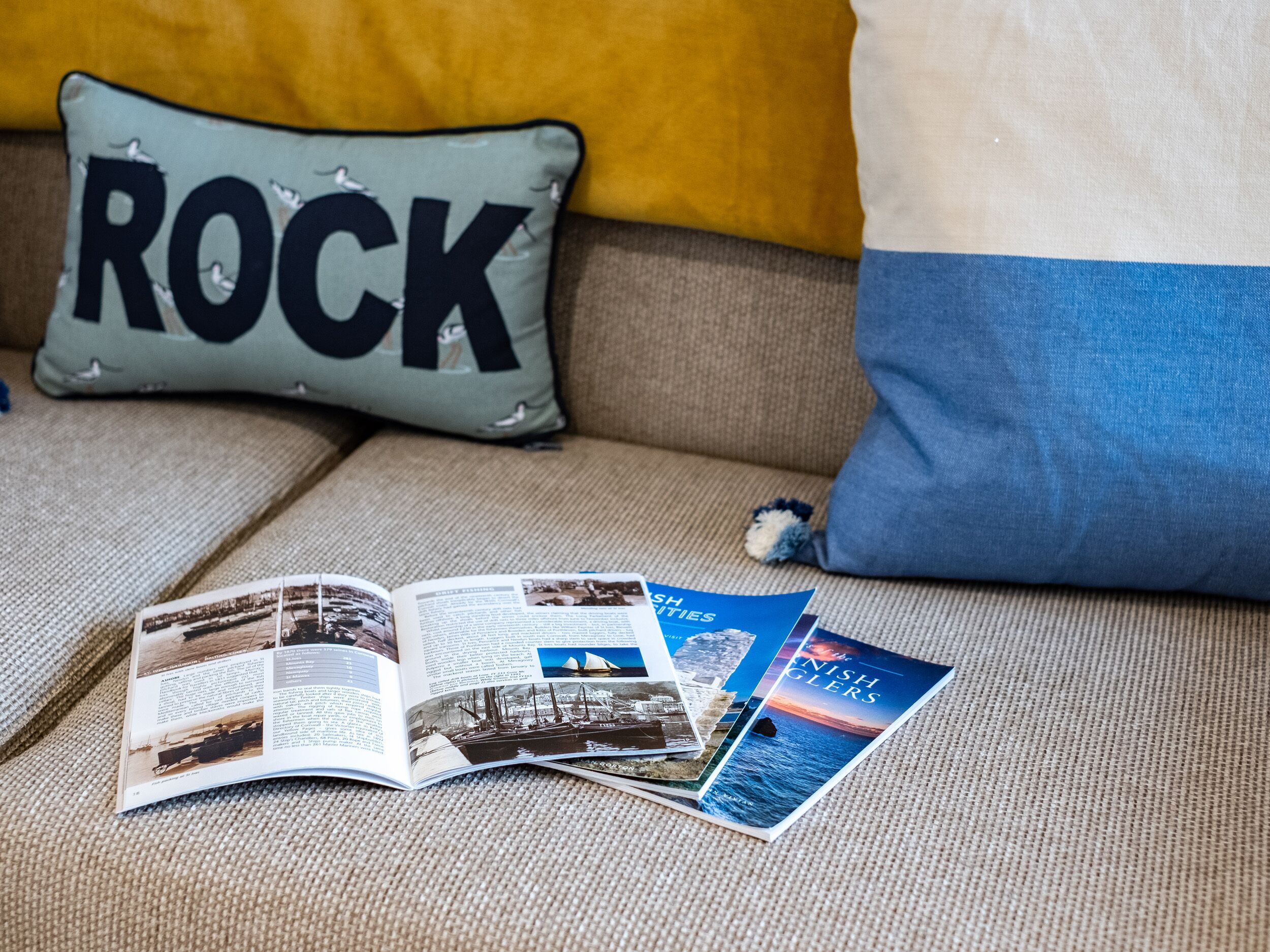 Uma revista aberta em um sofá, com um travesseiro com a inscrição 'ROCK'.