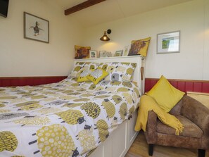 Uma cama com colcha estampada, um abajur, uma cadeira com manta e quadros nas paredes.