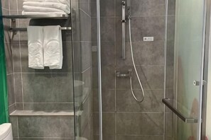 Um chuveiro com porta de vidro, um porta-toalhas com toalhas dobradas e um painel de controle de água visível.