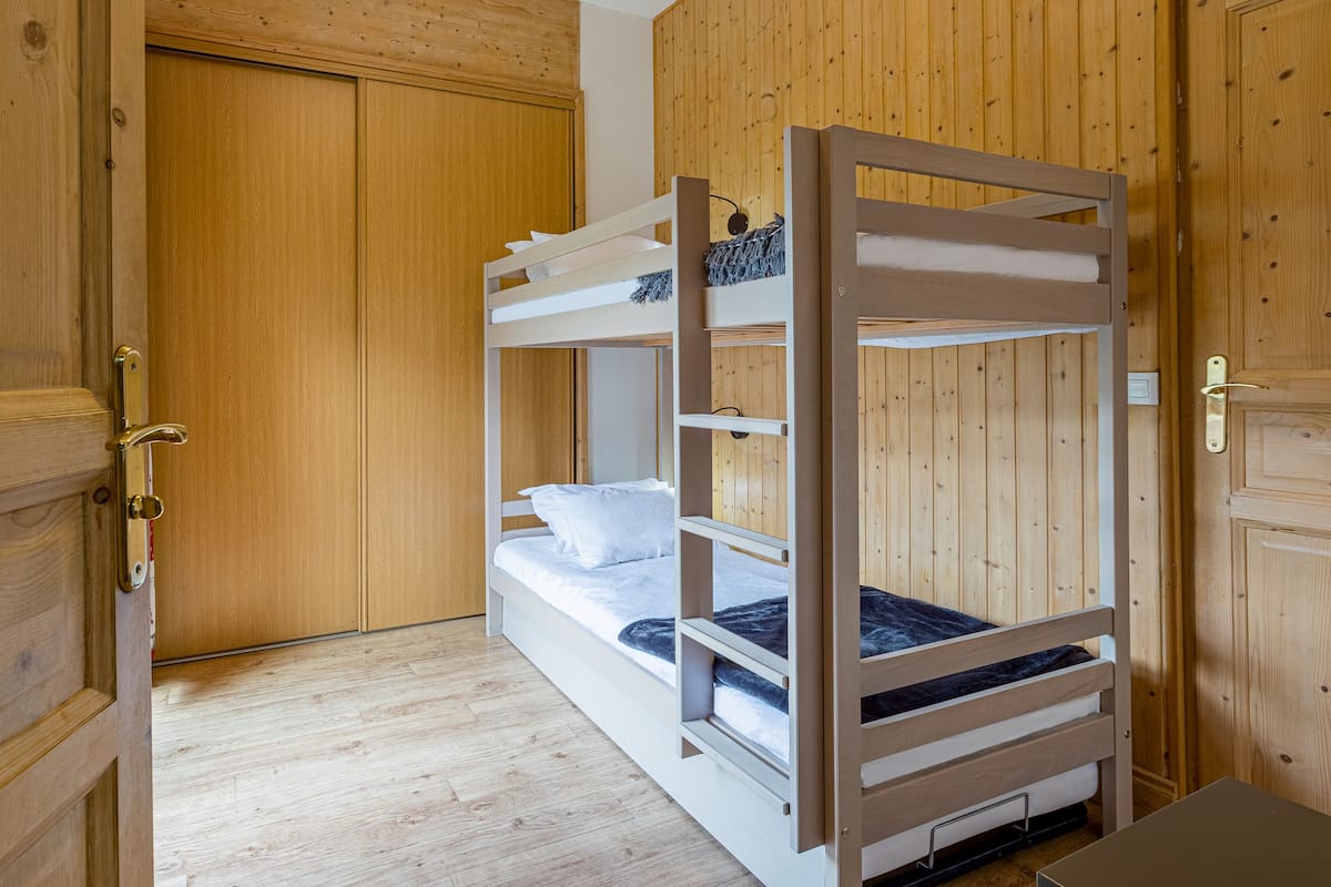 Quarto com beliches, paredes de madeira e uma porta.
