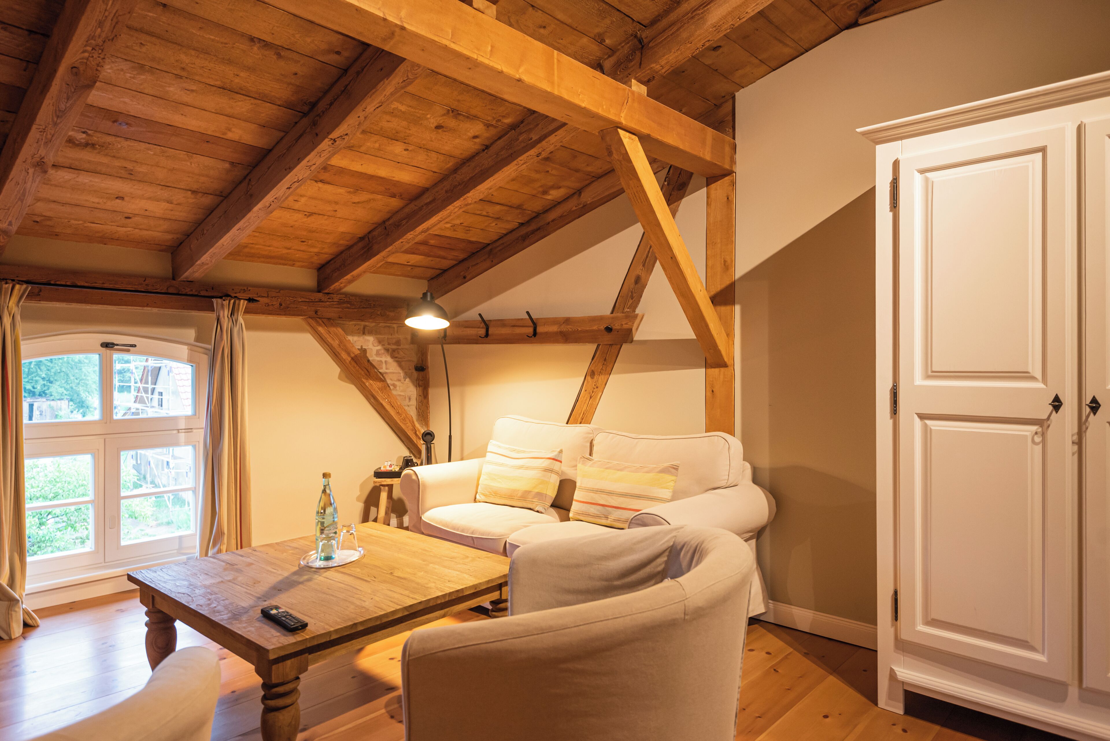 Um quarto acolhedor com teto de madeira, porta branca e janela com cortinas.