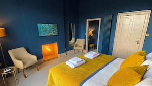 Quarto de hotel com cama, uma cadeira, lareira, porta e um quadro na parede.