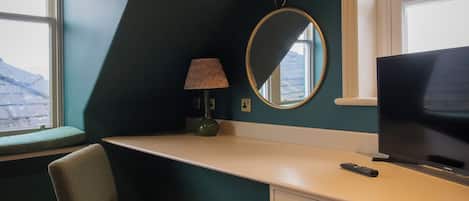 Quarto com escrivaninha, cadeira, televisão e janela com vista para montanhas.
