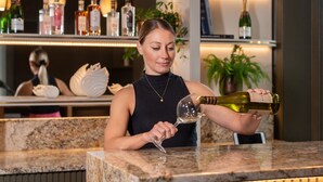 Uma pessoa servindo vinho em um copo em um bar, com prateleiras de garrafas ao fundo.