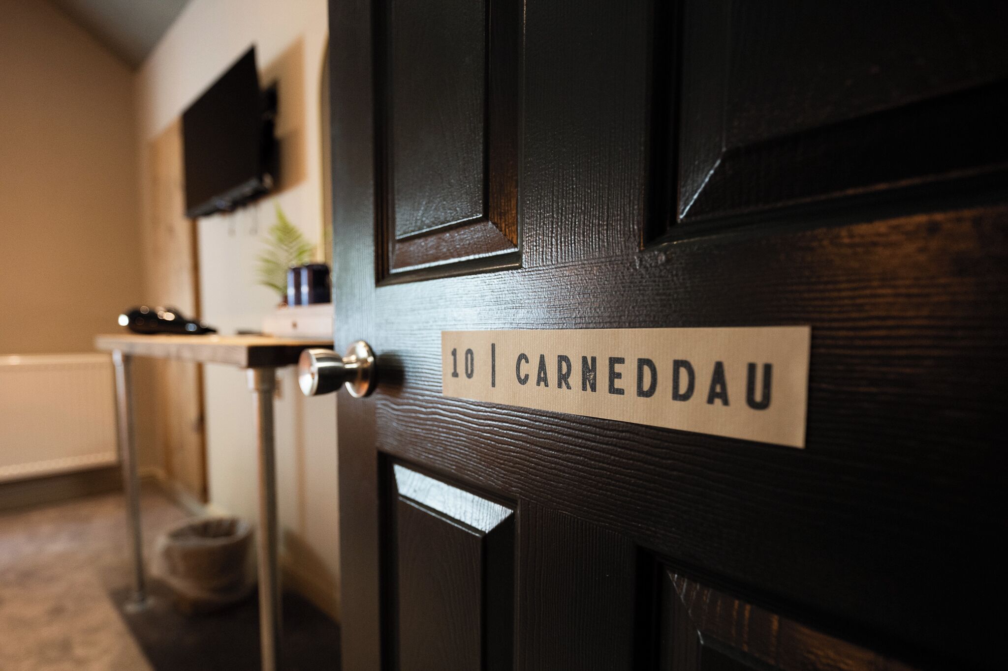 Uma porta com uma placa que diz '10 | CARNEDDAU' e uma televisão presa na parede acima.