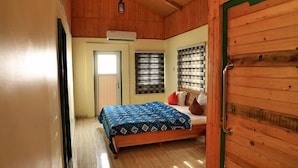 Quarto com teto de madeira, cama com colcha estampada, janela com persianas e porta com moldura verde.