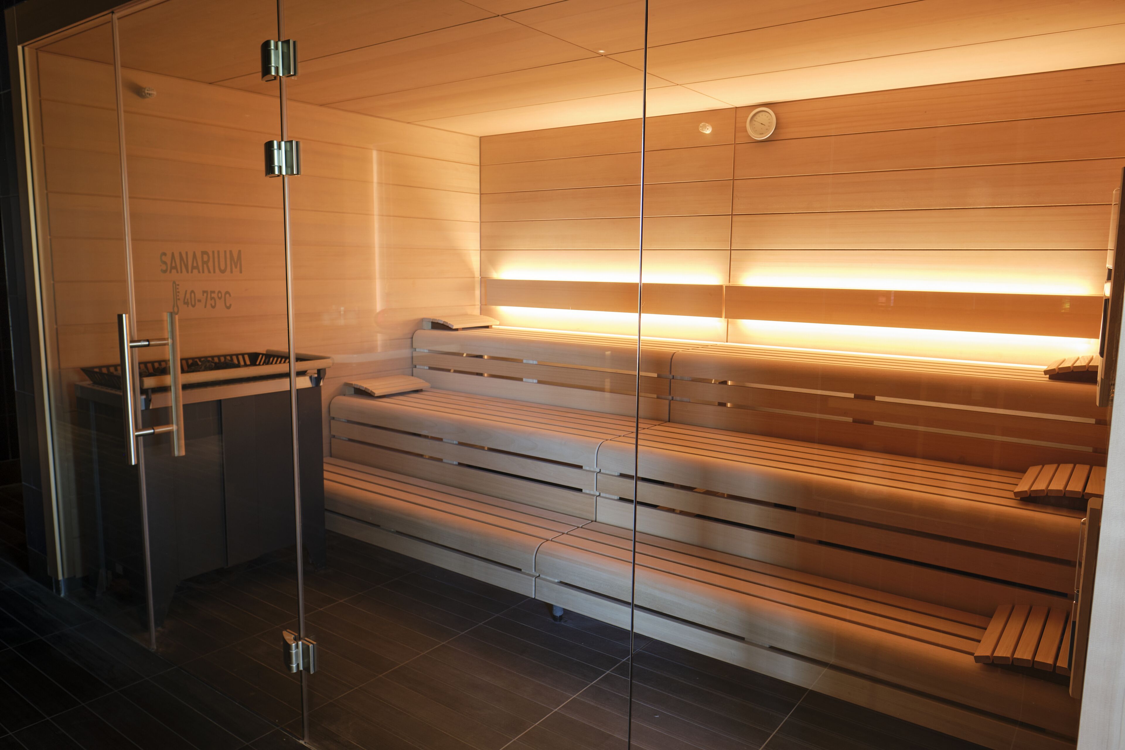 Uma sauna moderna com divisória de vidro, bancos de madeira e painel de controle.