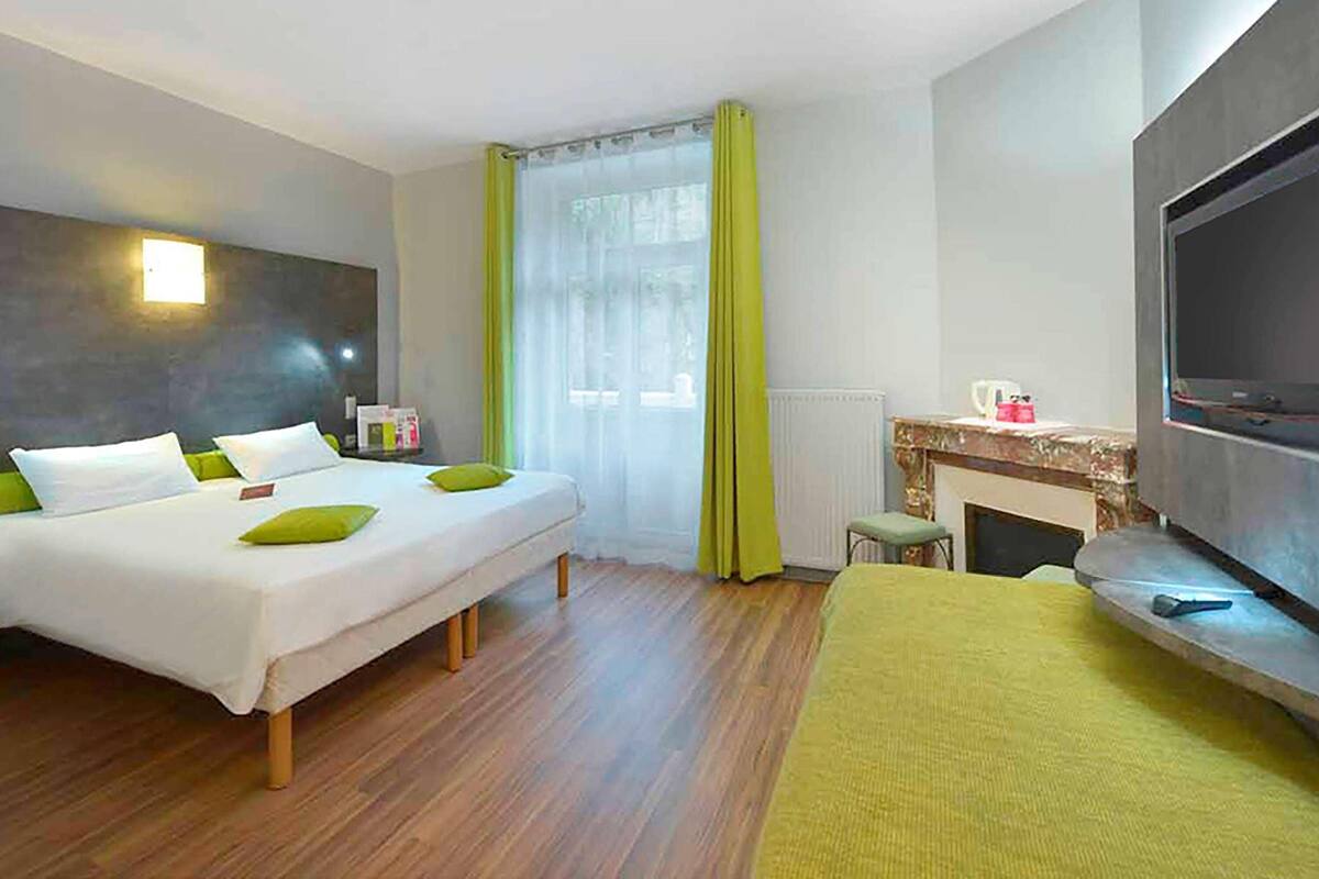 Quarto de hotel com cama, televisão, lareira e janela com cortinas.