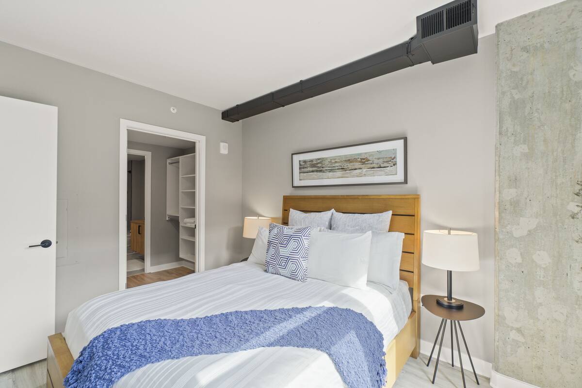 Um quarto com cama, abajur e um quadro na parede.