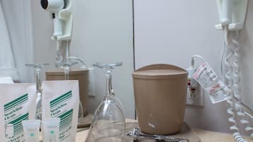 Uma casa de banho com secador de cabelo, frasco de champô, um copo e uma chávena no balcão.