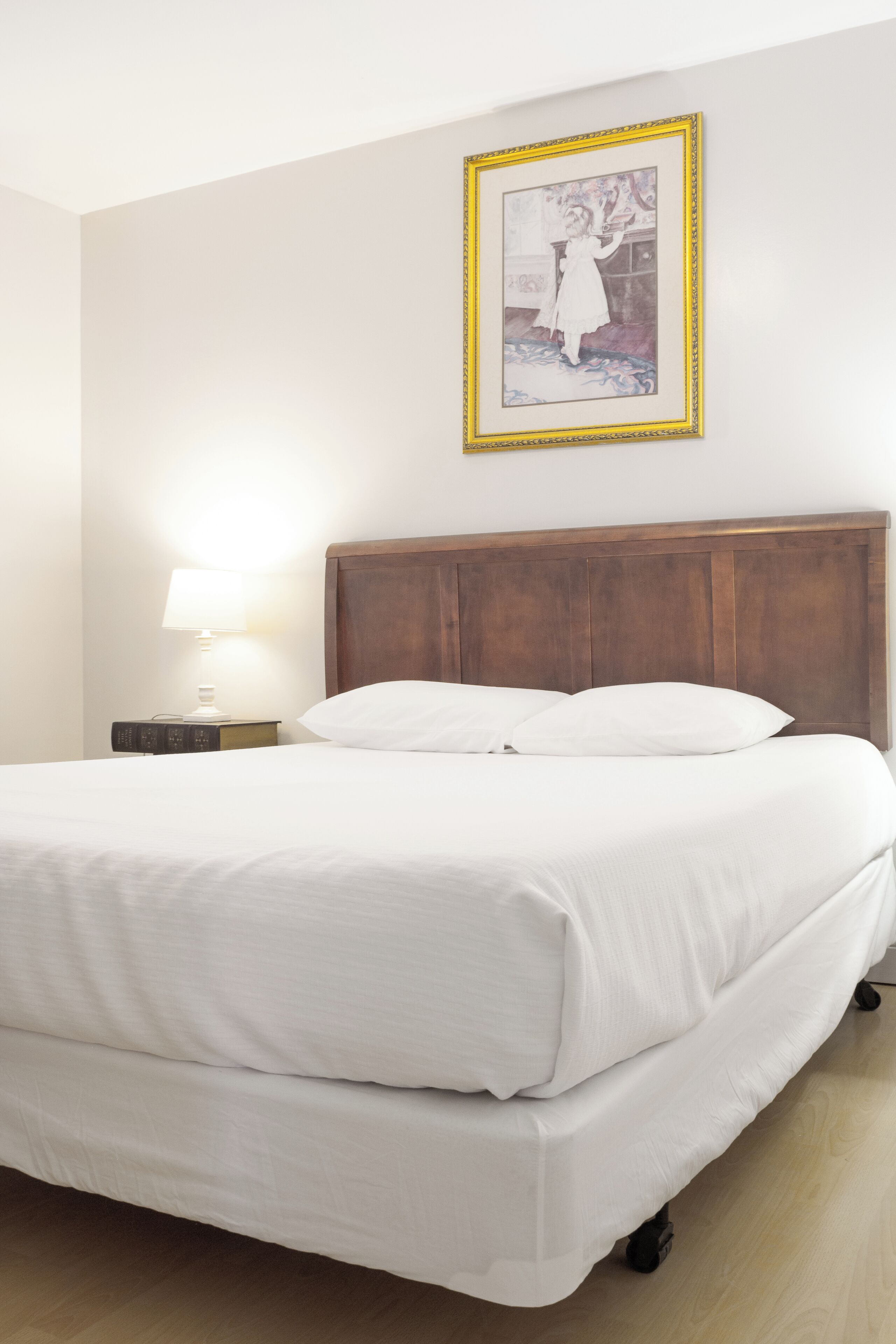 Cama bem arrumada com lençóis brancos, cabeceira de madeira e mesa de cabeceira com abajur.