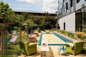 Pátio com área de estar externa, piscina e um edifício ao fundo.