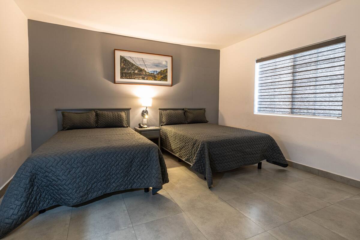 Quarto com duas camas, mesa de cabeceira, abajur, quadro pendurado na parede e janela com persianas.
