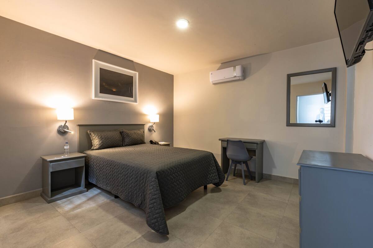 Quarto moderno com cama, abajures, escrivaninha e uma cadeira.