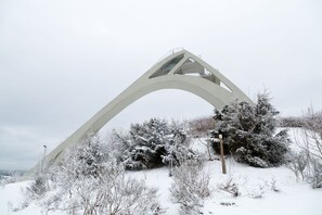 Uma grande estrutura de ponte branca e arqueada em meio a uma paisagem nevada com vegetação escassa.
