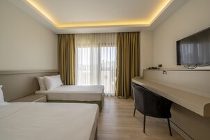 Quarto de hotel com duas camas, uma escrivaninha, uma cadeira, uma televisão e uma janela com cortinas.