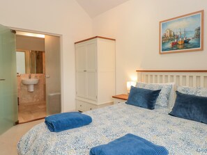 Quarto com cama, mesa de cabeceira, guarda-roupa, um quadro e banheiro visível por uma porta aberta.