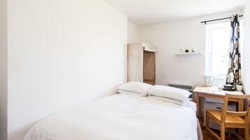 Quarto com cama, escrivaninha de madeira, cadeira, radiador e janela com cortinas.