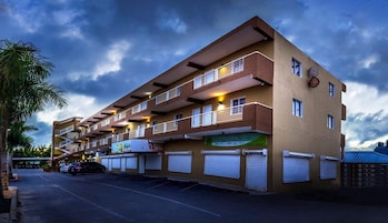 Um hotel com vários andares, varandas, área de estacionamento e um letreiro indicando um restaurante.