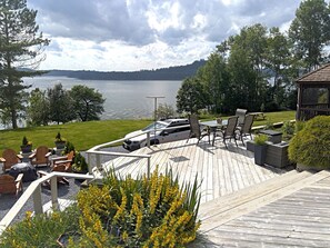 Um deck de madeira com mobiliário ao ar livre, com vista para um lago e colinas arborizadas.