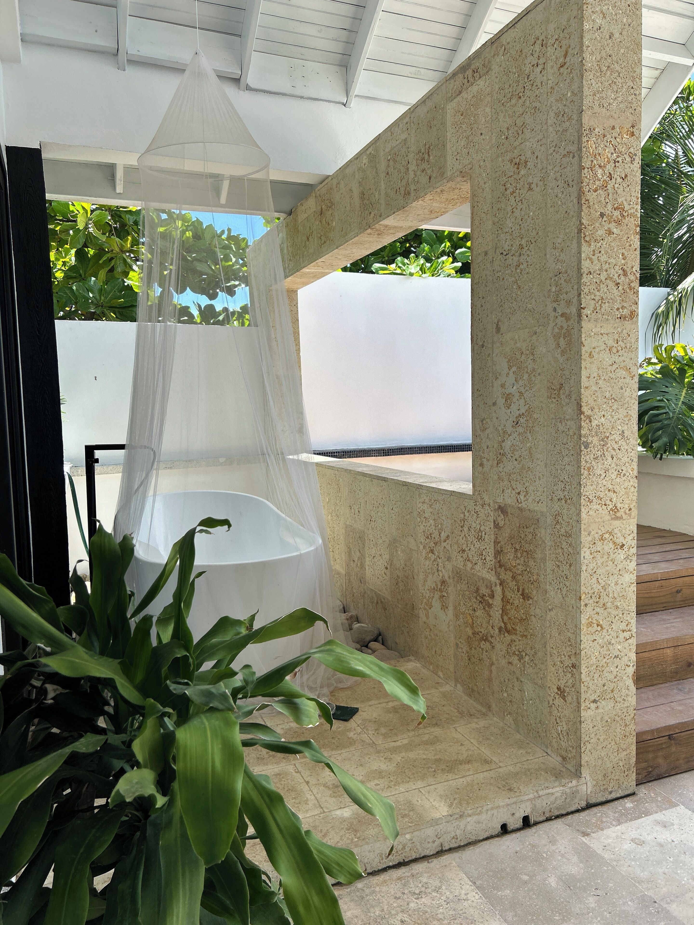 Uma área de estar moderna ao ar livre, com toldo branco e parede de pedra ao fundo.