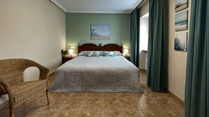 Um quarto com uma cama, uma cadeira, uma mesa de cabeceira, um abajur e um quadro na parede.