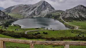 Paisagem montanhosa com um lago, uma estrada sinuosa e uma cerca de madeira.