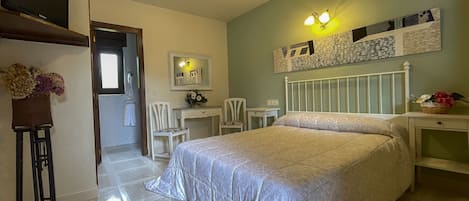 Quarto com cama, escrivaninha, cadeiras, espelho e luminária na parede.