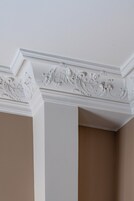Teto branco com molduras ornamentais e parede bege simples.