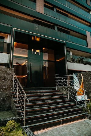 Um edifício moderno com entrada escura, escada com grades de metal e porta de vidro.