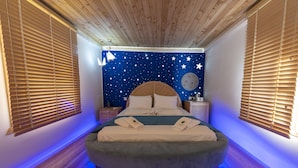 Quarto com mural da noite estrelada, cama redonda com cabeceira de madeira e persianas de madeira nas janelas.
