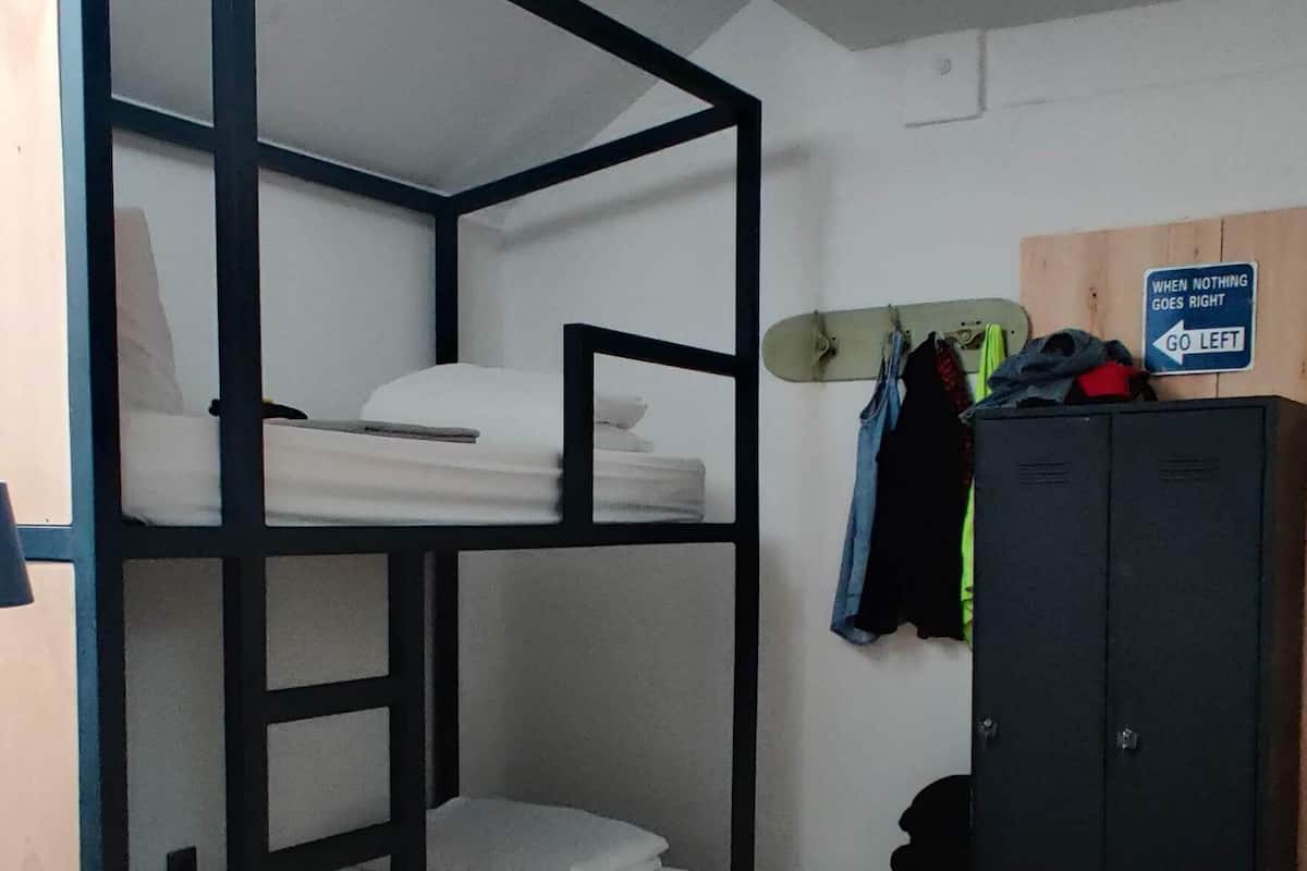 Uma cama beliche com um skate e roupas na parede, um guarda-roupa e um aviso na parede.