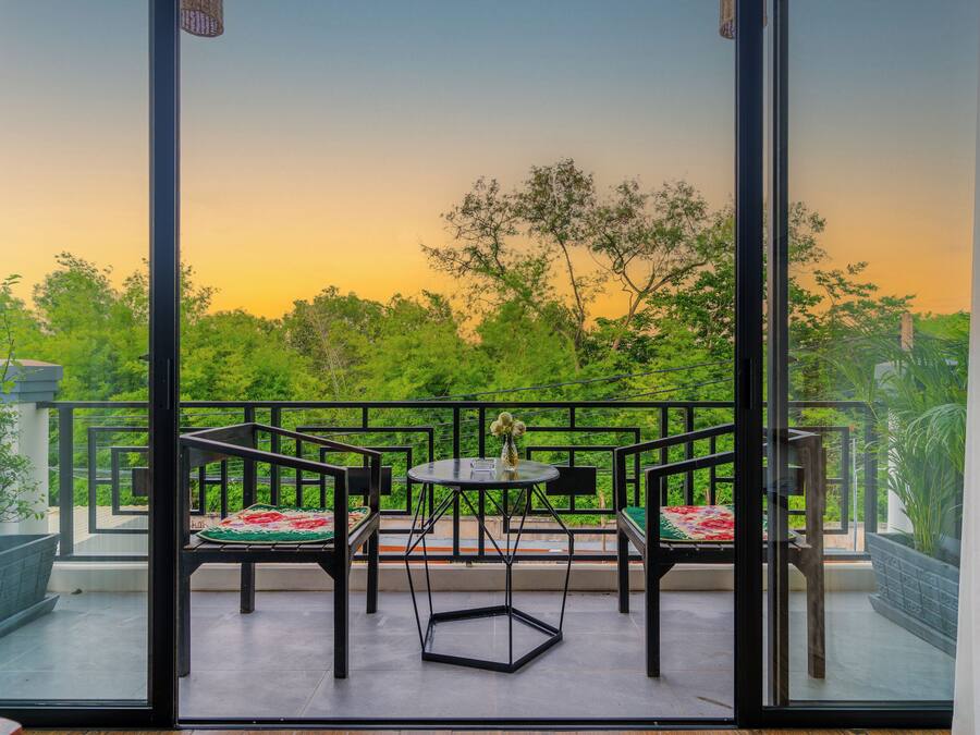Varanda com mesa e cadeiras, vista para o verde e um pôr do sol.