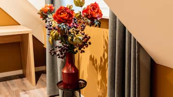 Um vaso vermelho com flores sobre uma pequena mesa em um quarto com piso de madeira e uma escada.