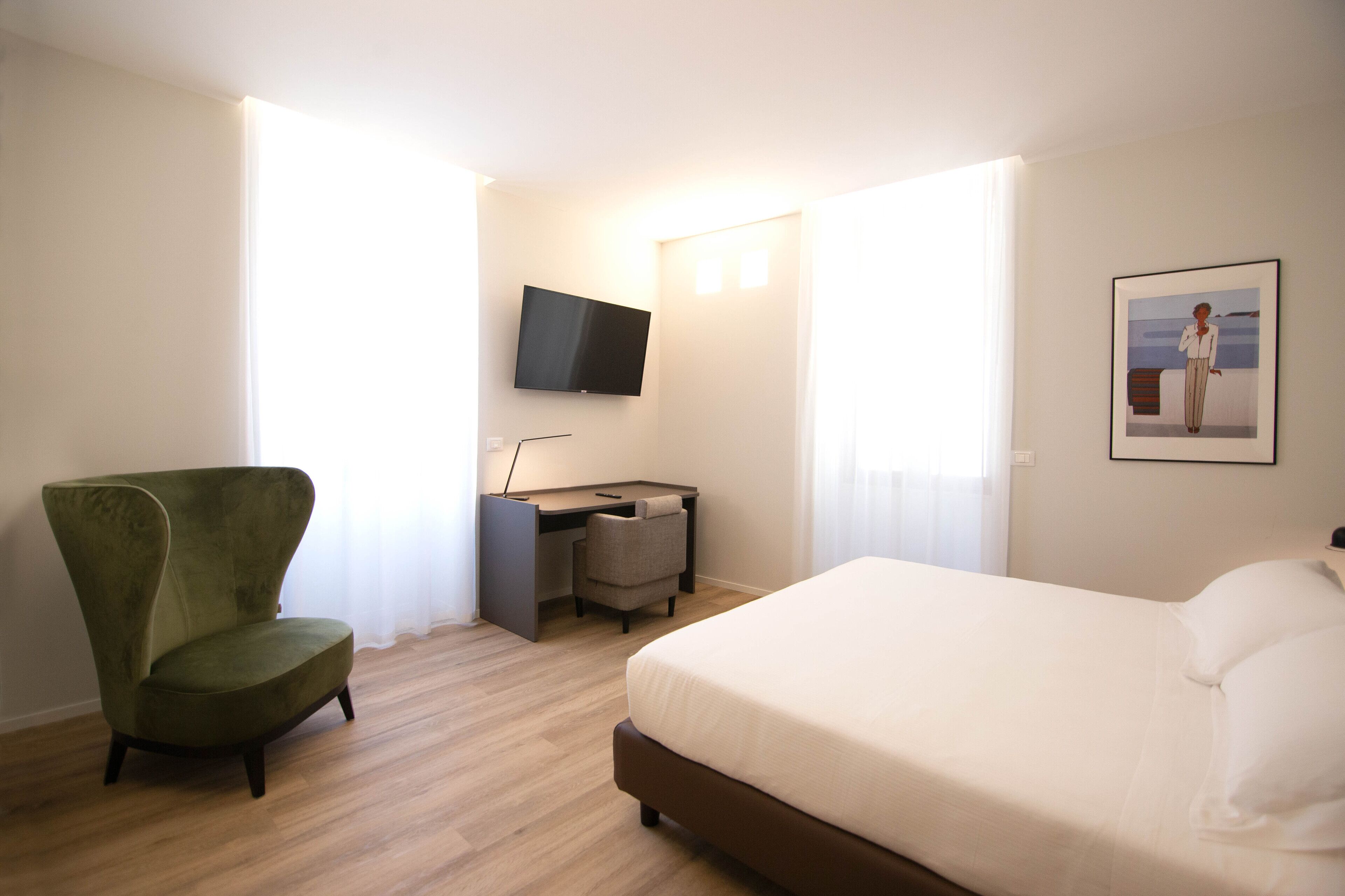 Quarto de hotel com cama, escrivaninha, cadeira, televisão e quadro na parede.