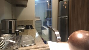 Cozinha com eletrodomésticos de aço inoxidável, bancada de granito e vista para o aposento vizinho.