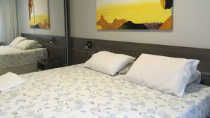Quarto de hotel com uma cama grande, uma cama menor, um espelho e um quadro de uma paisagem de montanhas.