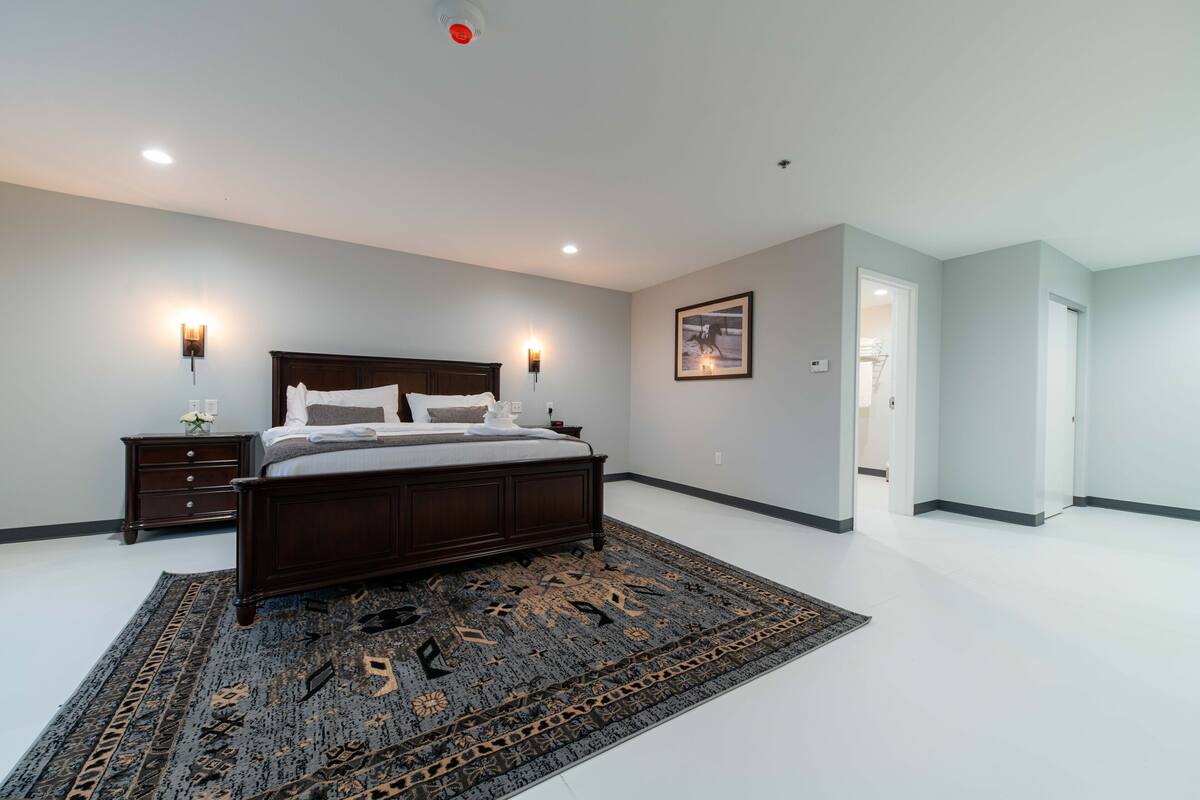 Quarto com cama grande, mesas de cabeceira, tapete e um quadro na parede.